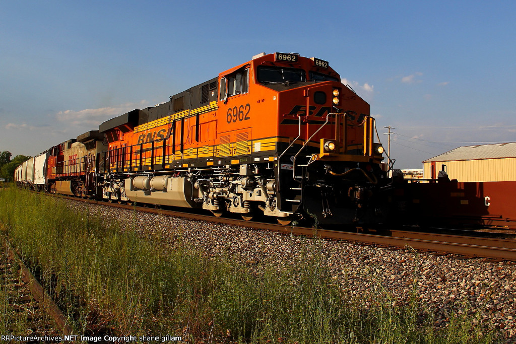 BNSF 6962 heads Sb while passing a baretable in the siding.